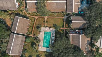 Vista aérea de uma área residencial com várias casas, uma piscina central e vegetação ao redor.