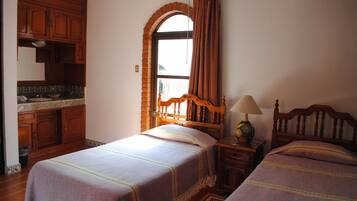 Quarto com duas camas, uma cabeceira de madeira, mesa de cabeceira com abajur e janela com cortinas.