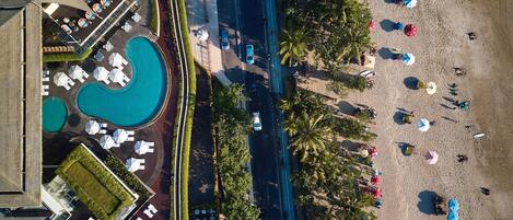 Vista aérea de um resort com piscina, área de praia com guarda-sóis e estacionamento.
