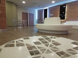 Um interior moderno com um sofá branco, uma mesa com tampo de vidro e uma área de jantar com cadeiras.