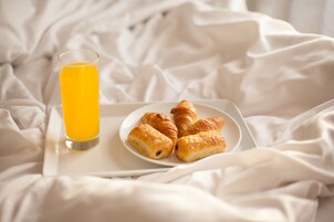 Uma bandeja com croissants e um copo de suco de laranja sobre uma cama com lençóis brancos.