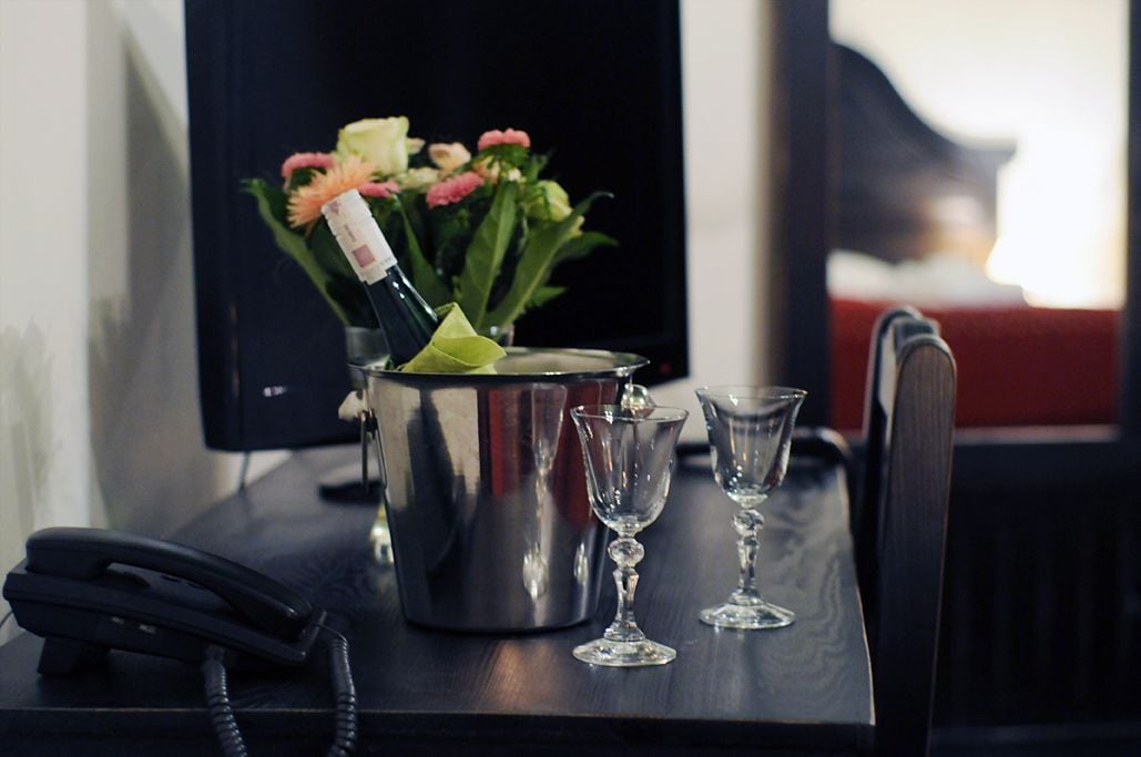Quarto de hotel com escrivaninha, telefone, uma garrafa de champanhe e duas taças de vinho.