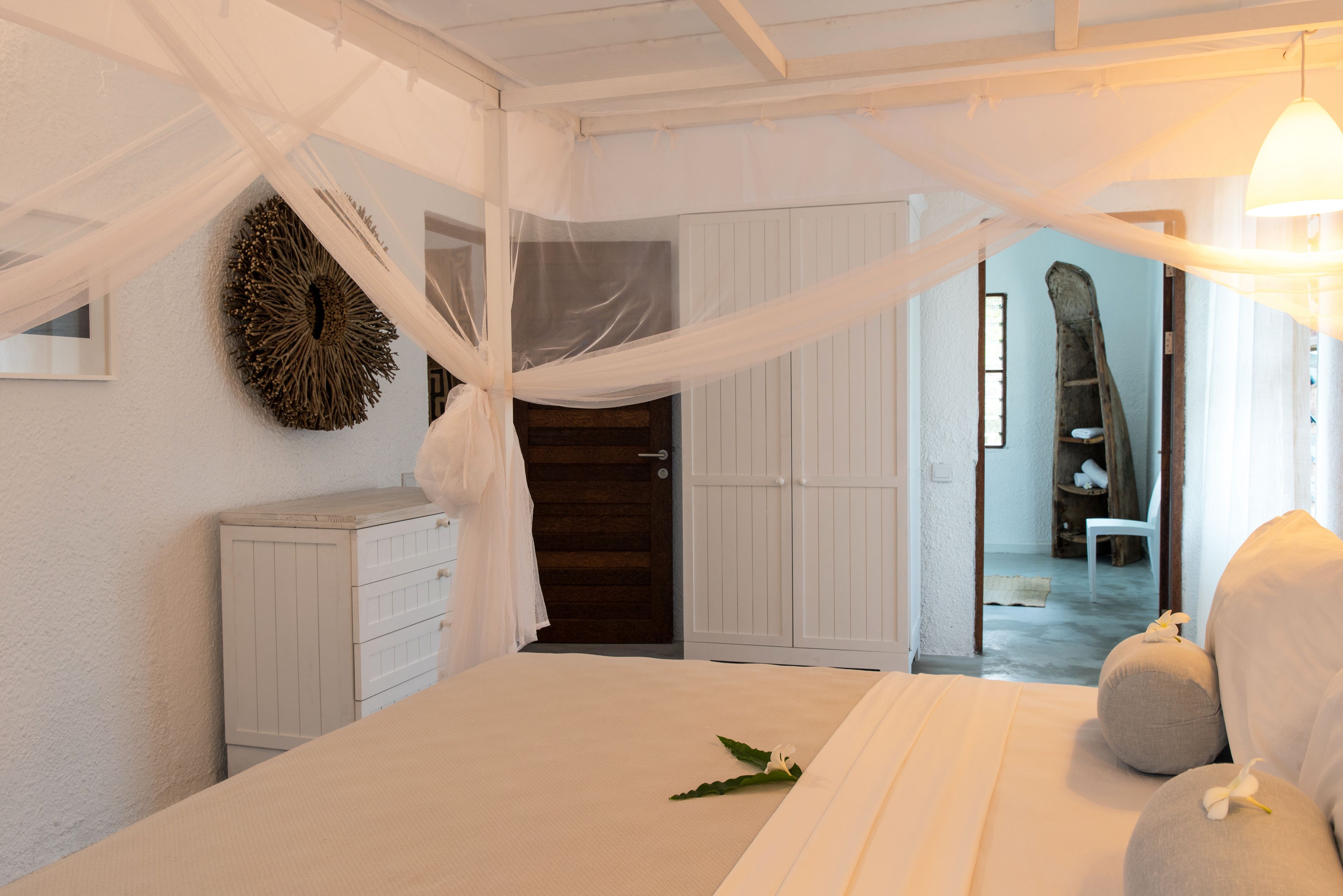 Quarto com cama, guarda-roupa, espelho e porta que dá para outro cômodo.