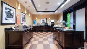 Uma cozinha de hotel com piso xadrez, armários de madeira escura e um balcão de buffet com alimentos.