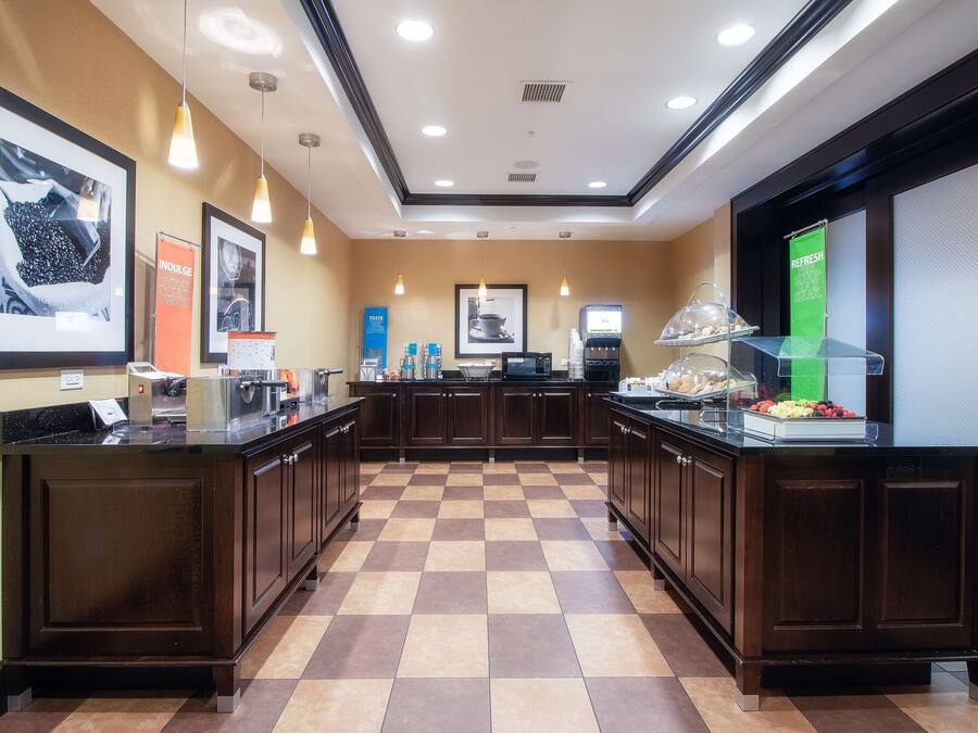 Uma cozinha de hotel com piso xadrez, armários de madeira escura e um balcão de buffet com alimentos.