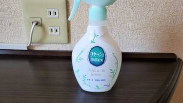 Um frasco de amaciante de tecidos e aromatizador de ambiente com borrifador, apoiado em uma superfície de madeira contra uma parede texturizada.
