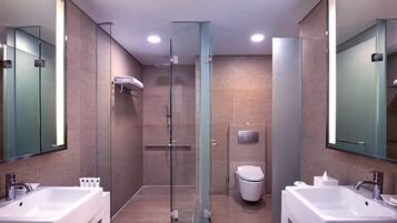 Um banheiro moderno com duas pias, box de vidro para o chuveiro e vaso sanitário.