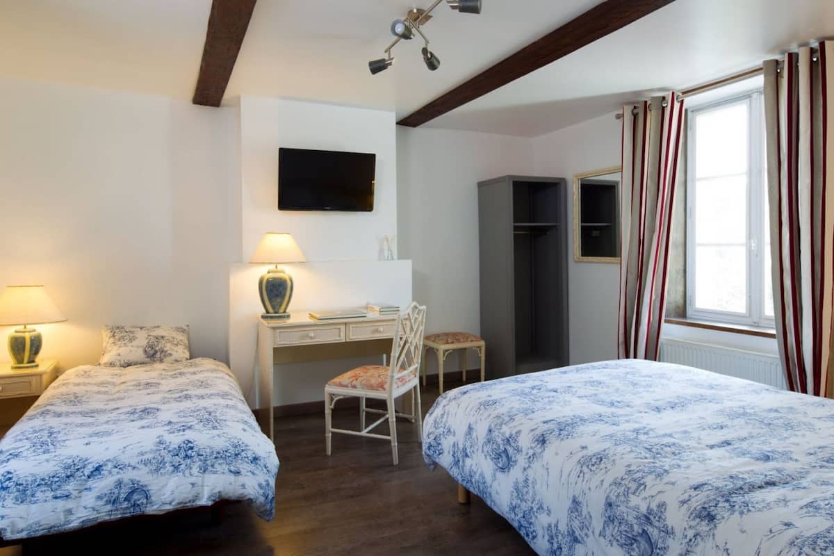 Quarto com duas camas, uma escrivaninha, uma cadeira, televisão e guarda-roupa.