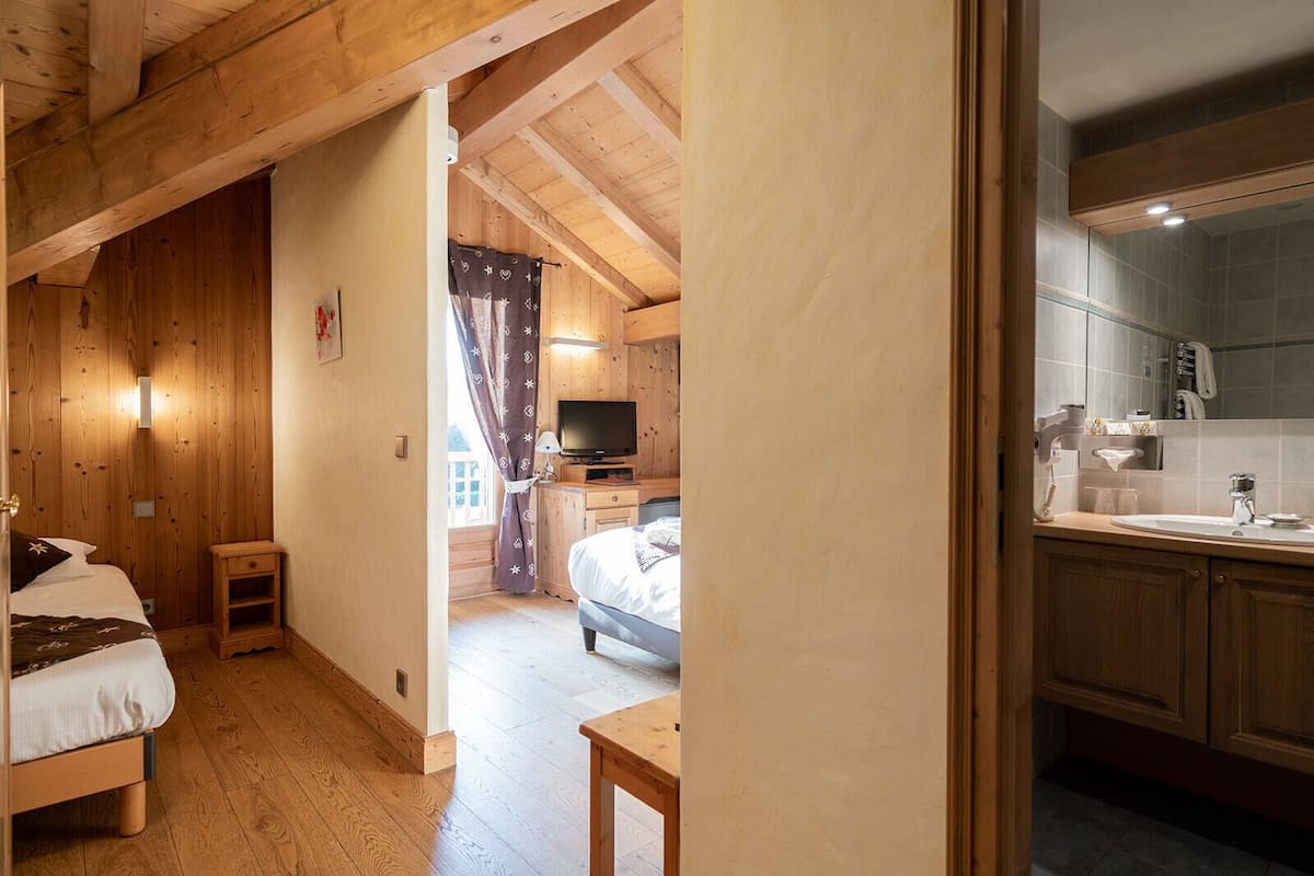 Quarto aconchegante com paredes de madeira, uma cama, uma mesa pequena e uma TV no canto.