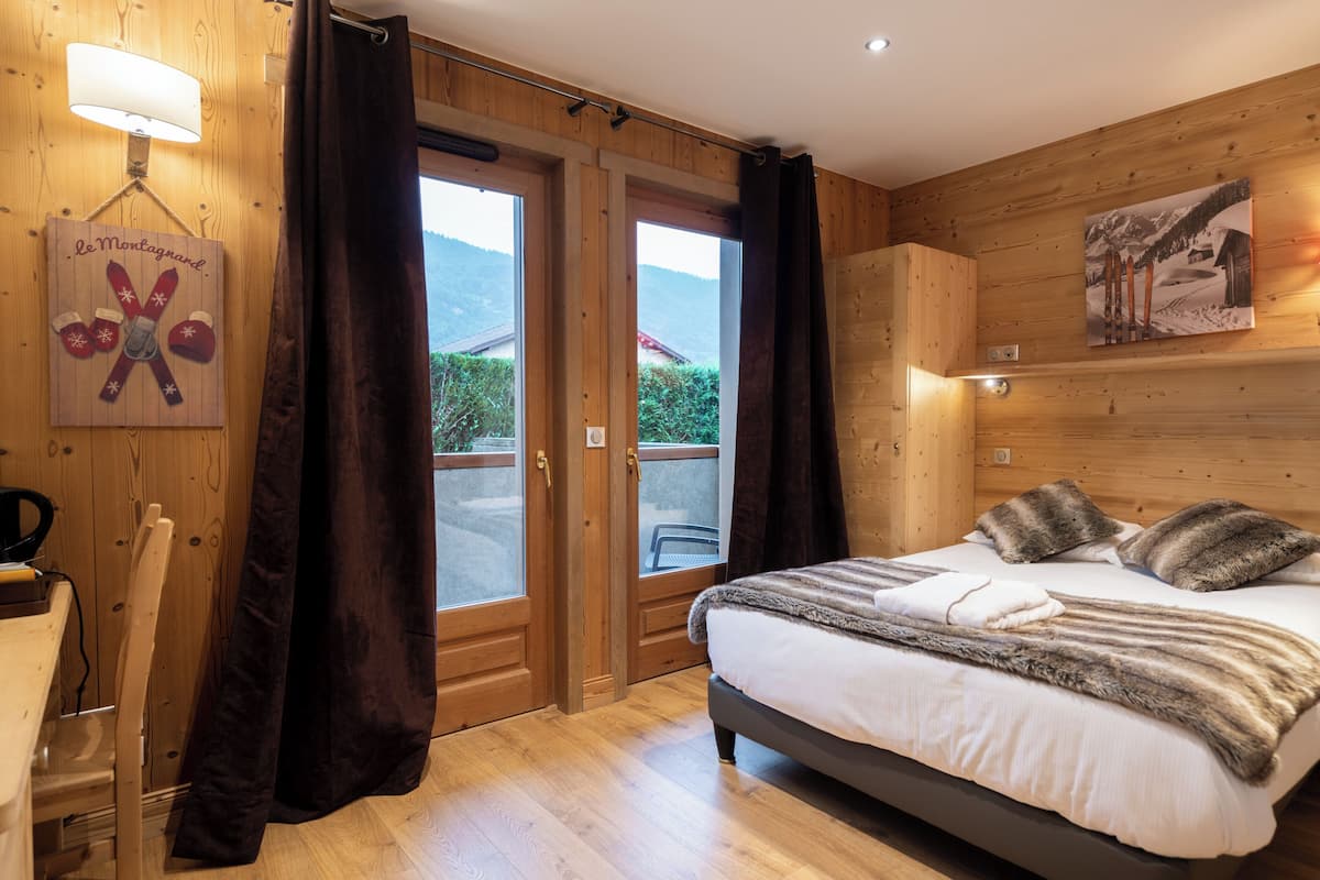 Um quarto com painéis de madeira, uma cama, um abajur, uma janela e uma porta.
