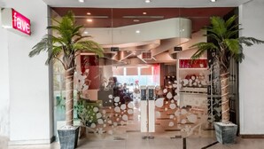 Uma entrada de hotel moderna com portas de vidro, palmeiras e um letreiro que diz 'fave'.