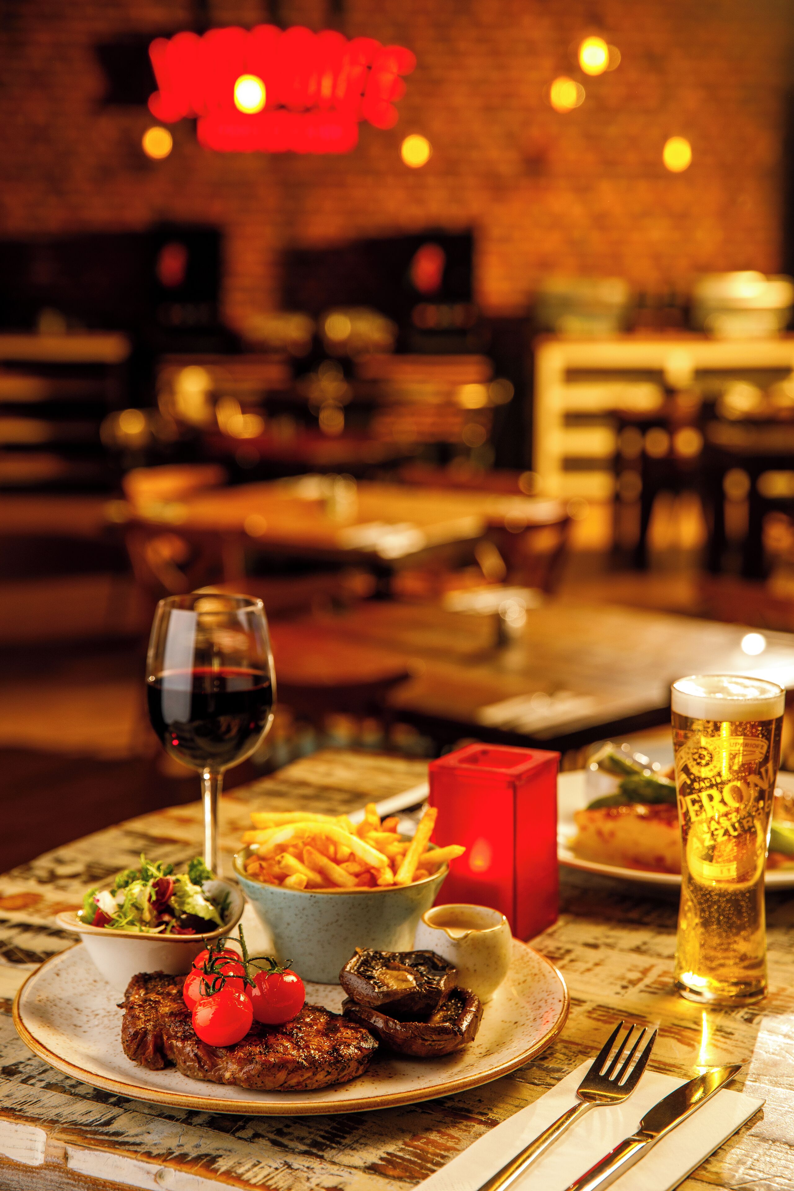 Um ambiente de restaurante com um prato de comida, um copo de vinho tinto e uma caneca de cerveja.