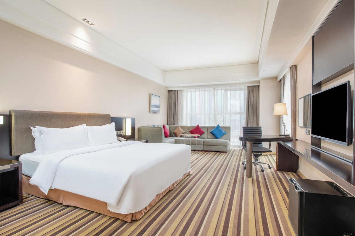 Quarto de hotel com cama grande, escrivaninha, televisão de tela plana, sofá e poltrona.