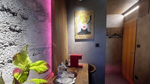 Um balcão de receção em madeira, com uma planta, um quadro e uma cadeira vermelha, num interior moderno com paredes texturizadas e uma porta de madeira.