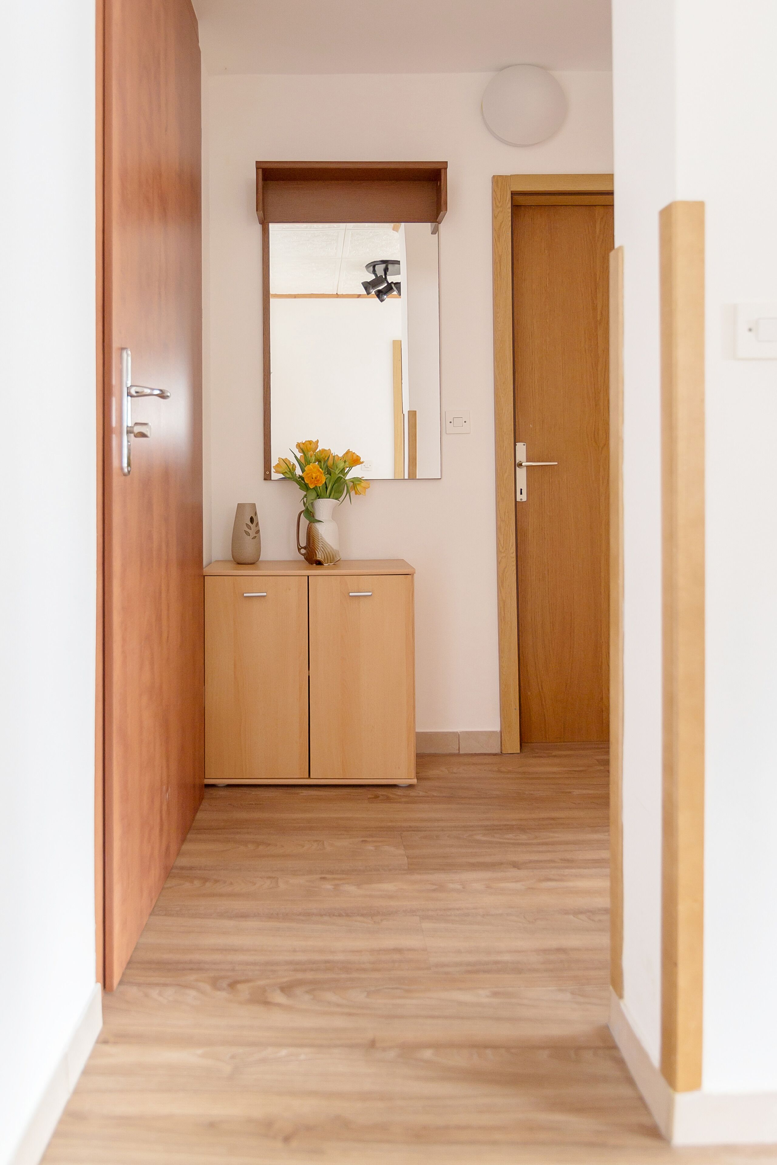 Um corredor com assoalho de madeira, guarda-roupa de madeira, um espelho e um vaso com flores.