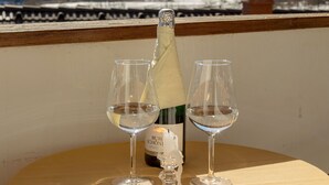 Uma mesa com uma garrafa de vinho e duas taças em uma varanda com vista para montanhas cobertas de neve.