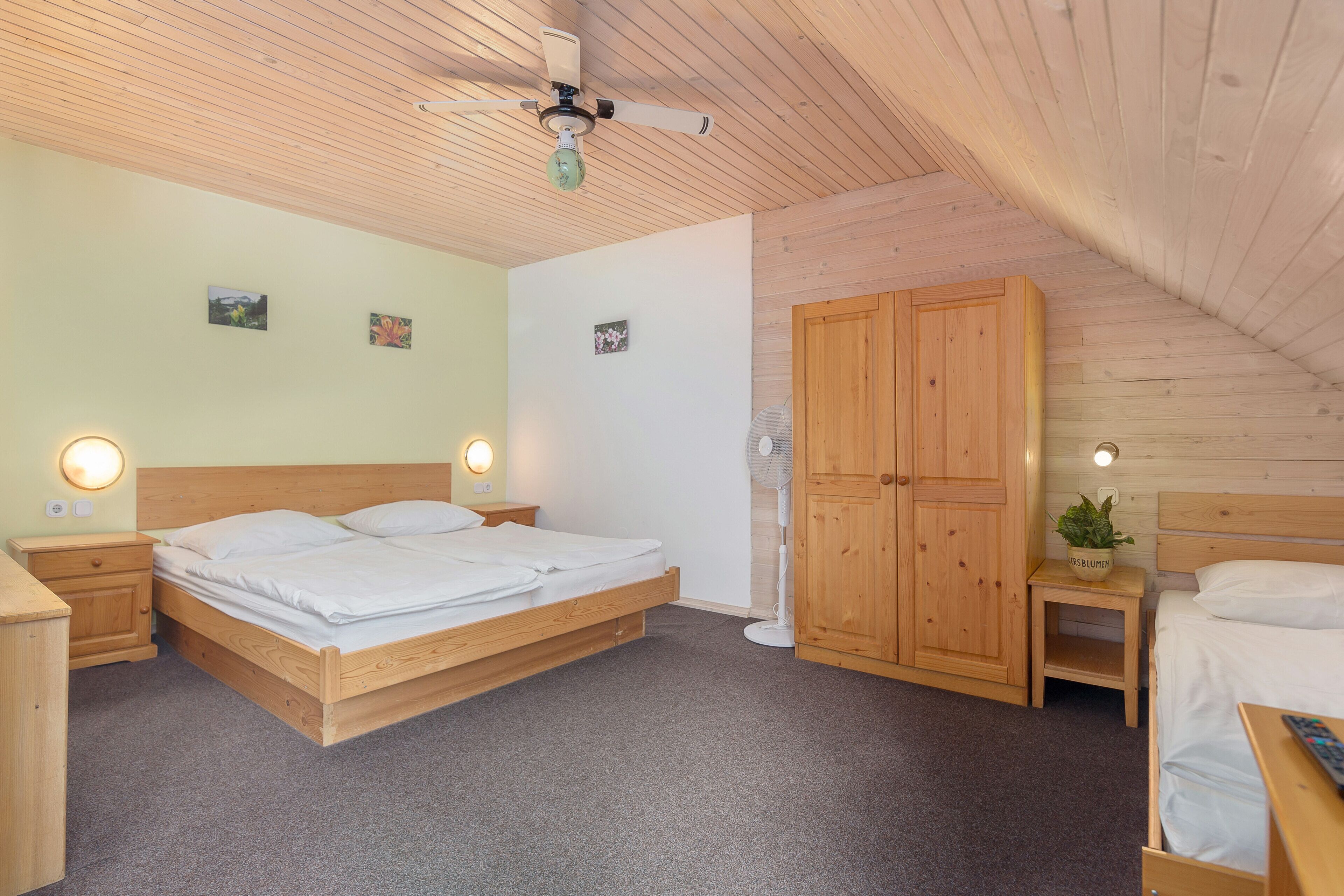 Quarto com cama de madeira, mesas de cabeceira, ventilador de teto e guarda-roupa.