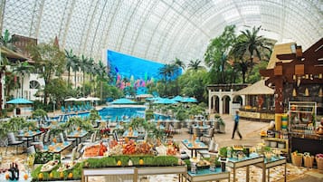 Amplo espaço interno com uma piscina grande, mesas de jantar e plantas tropicais.