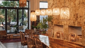 Uma sala de jantar com mesa de madeira e cadeiras de vime, parede de pedra e luminárias de vime suspensas.