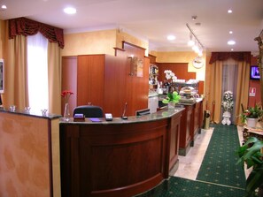 Um saguão de hotel com uma mesa de recepção, um espaço de bar e um chão coberto por um tapete verde.
