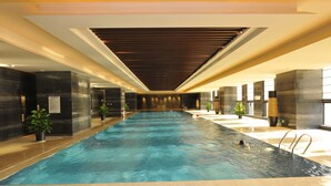 Piscina interior com água cristalina, ladeada por paredes de pedra escura e vasos com plantas.