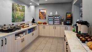 Uma cozinha moderna com bancada de mármore, cafeteira, frigorífico e micro-ondas.