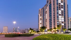 Um edifício alto com várias varandas, rodeado por jardins bem cuidados e iluminação pública.