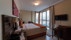 Quarto de hotel com uma cama grande, televisão, escrivaninha e janela com vista para a cidade.