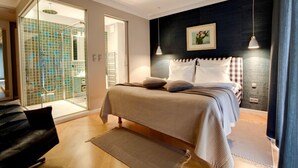 Quarto com cama, luminárias de cabeceira, uma janela ampla e área de chuveiro com portas de vidro.