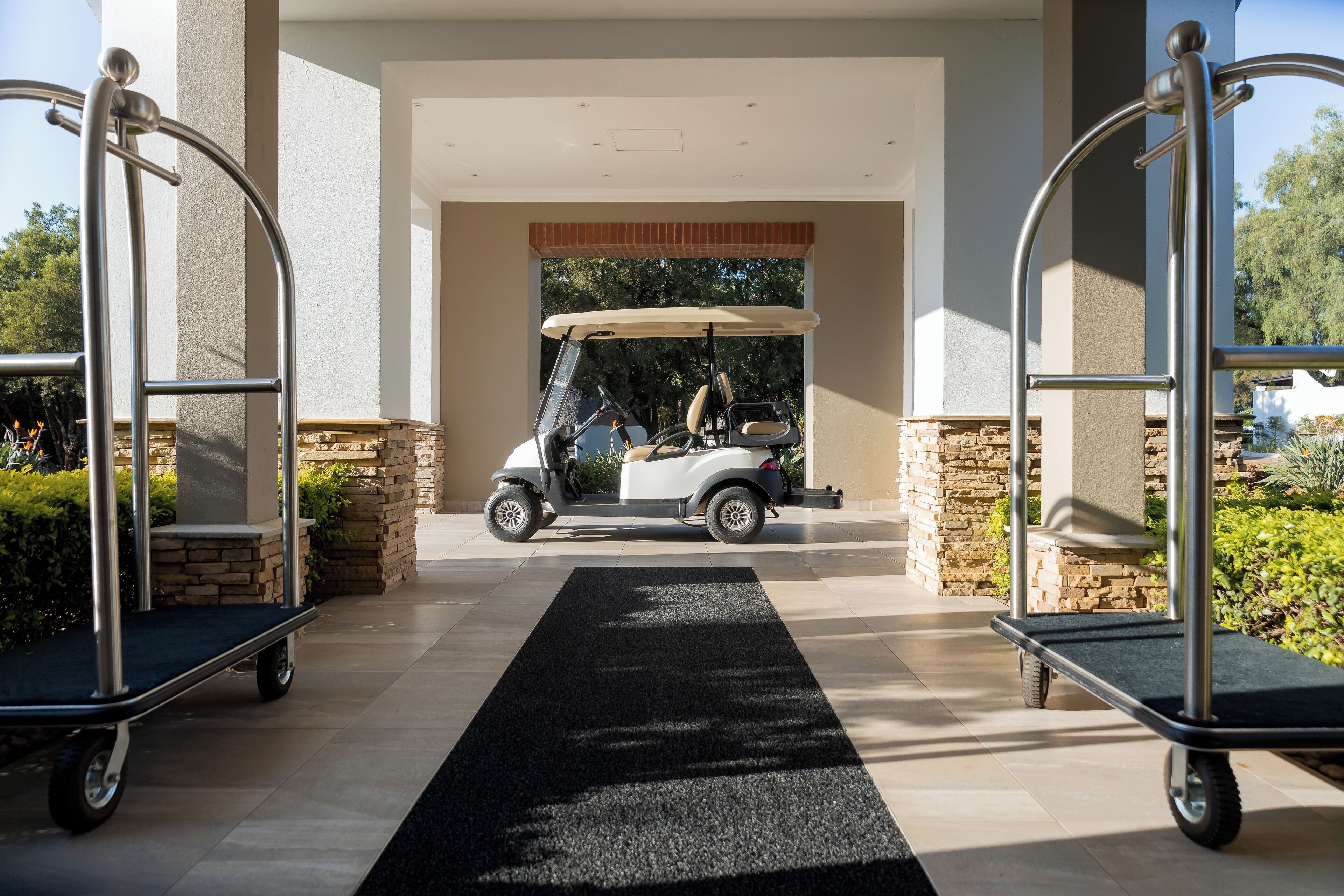 Carrinho de golfe numa área de entrada coberta, com um tapete preto a levá-lo até ele.