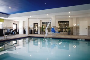Piscina interna com posto de salva-vidas, espreguiçadeiras e área ao redor da piscina desimpedida.