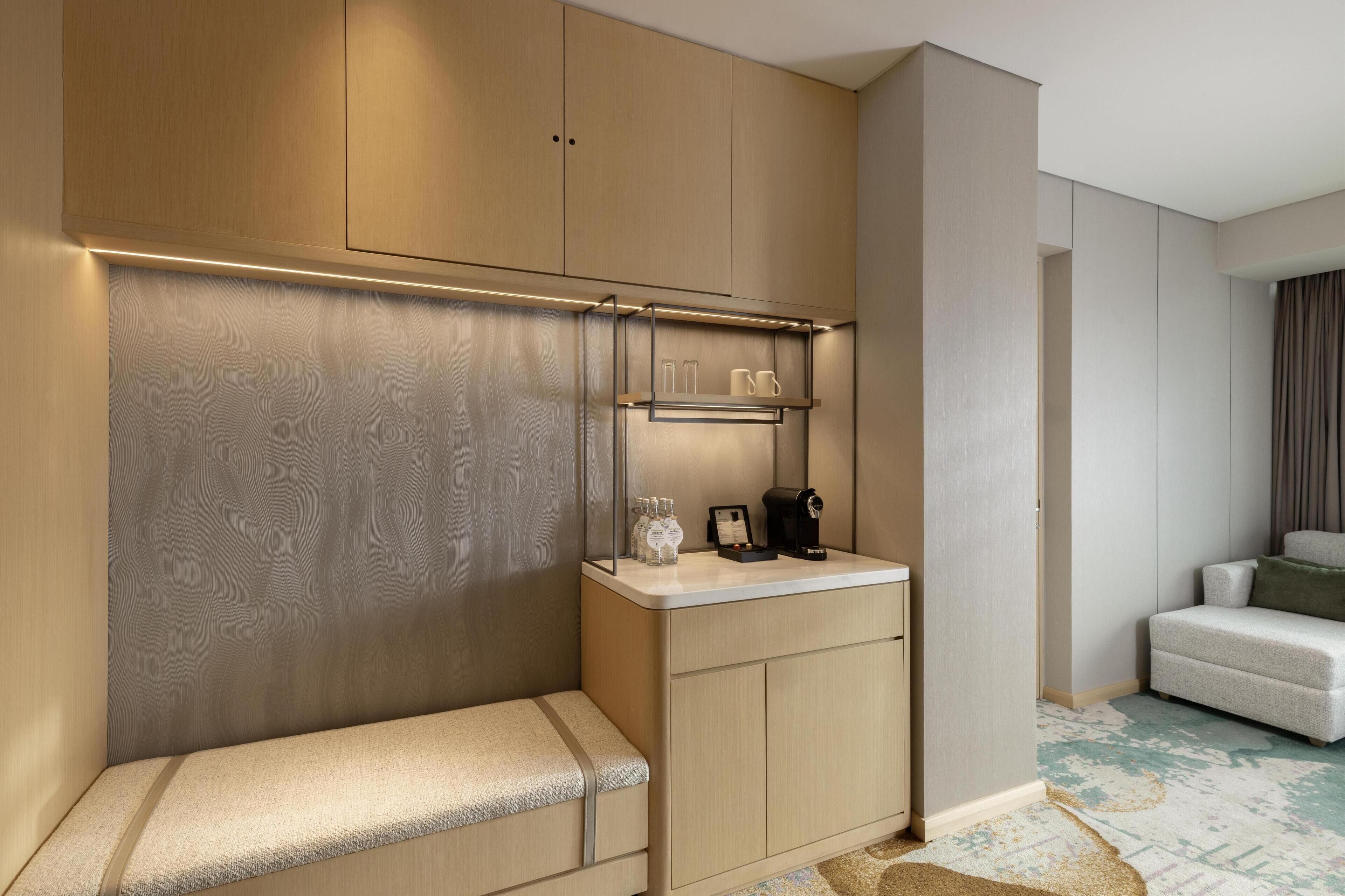 Quarto de hotel compacto com um banco embutido, pequena kitchenette e área de estar.
