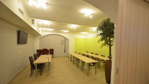 Uma sala de conferência com uma mesa comprida, cadeiras, um relógio e um vaso de planta.