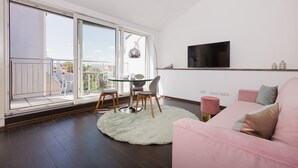 Uma sala de estar moderna com uma porta de vidro que dá para uma varanda, uma TV de tela plana na parede e um sofá rosa.