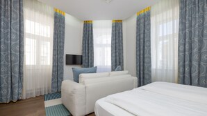 Quarto de hotel com cama, sofá, televisão e cortinas estampadas.