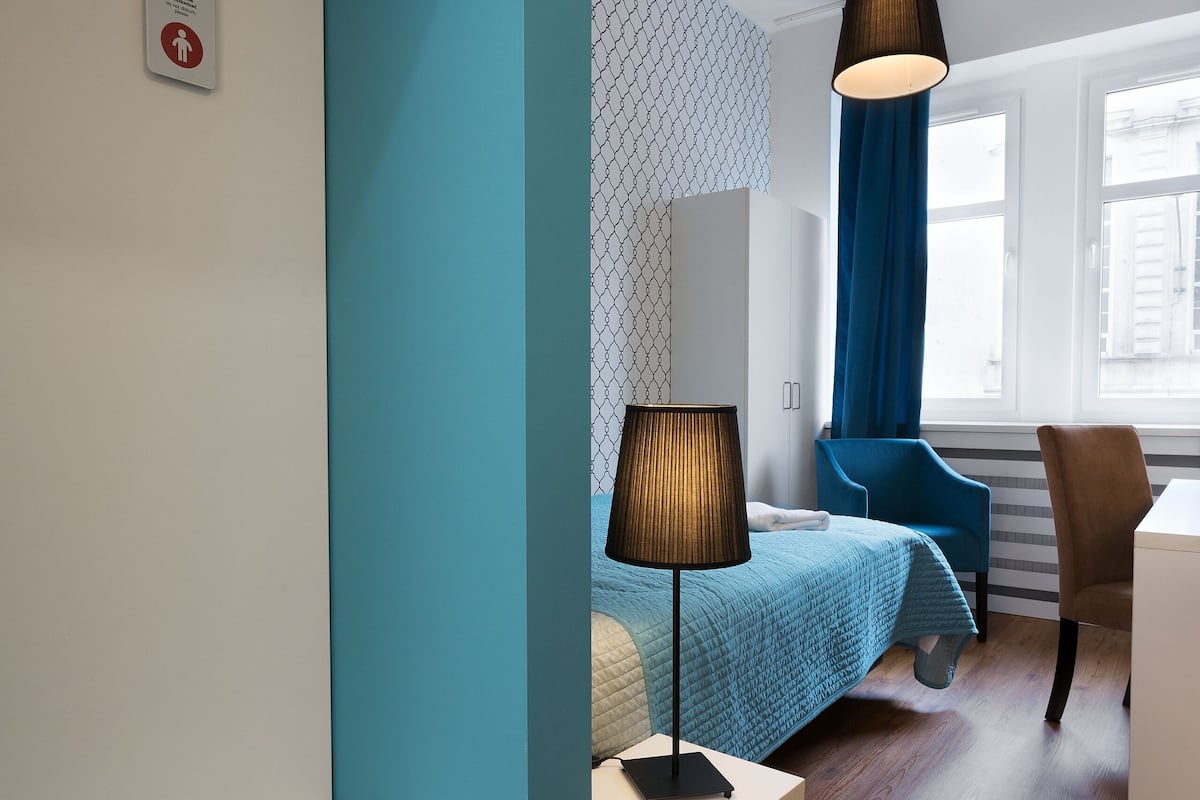 Quarto de hotel moderno com cama, escrivaninha, cadeira, abajur e janela.