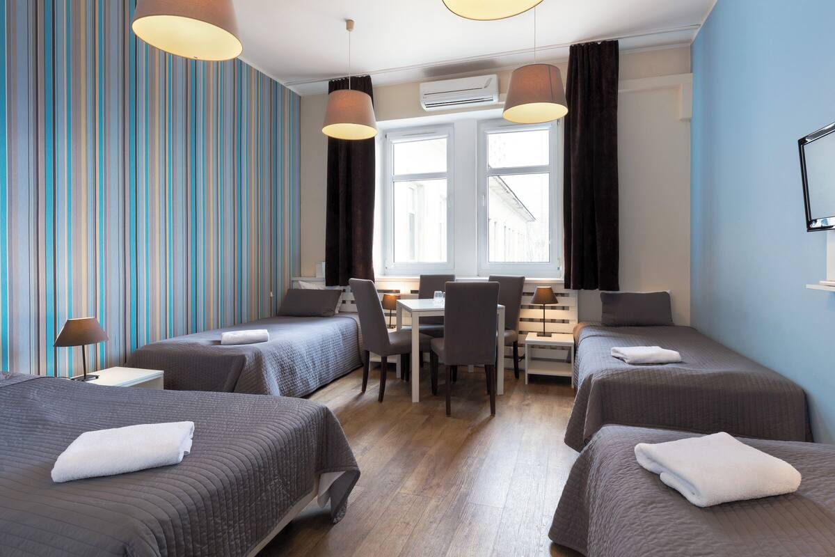 Quarto de hotel com duas camas de solteiro, uma escrivaninha e uma cadeira.