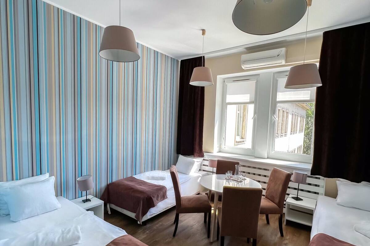 Quarto de hotel com parede listrada, mesa de jantar com cadeiras e várias camas.