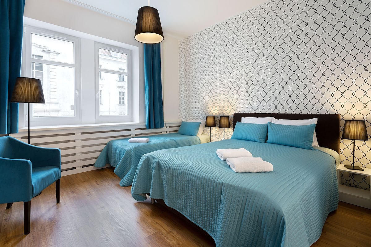 Quarto de hotel com duas camas, uma cadeira e uma janela com cortinas.