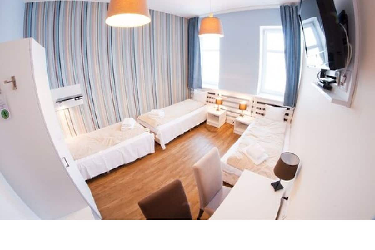 Quarto de hotel com duas camas de solteiro, uma escrivaninha, uma cadeira e uma televisão fixada na parede.