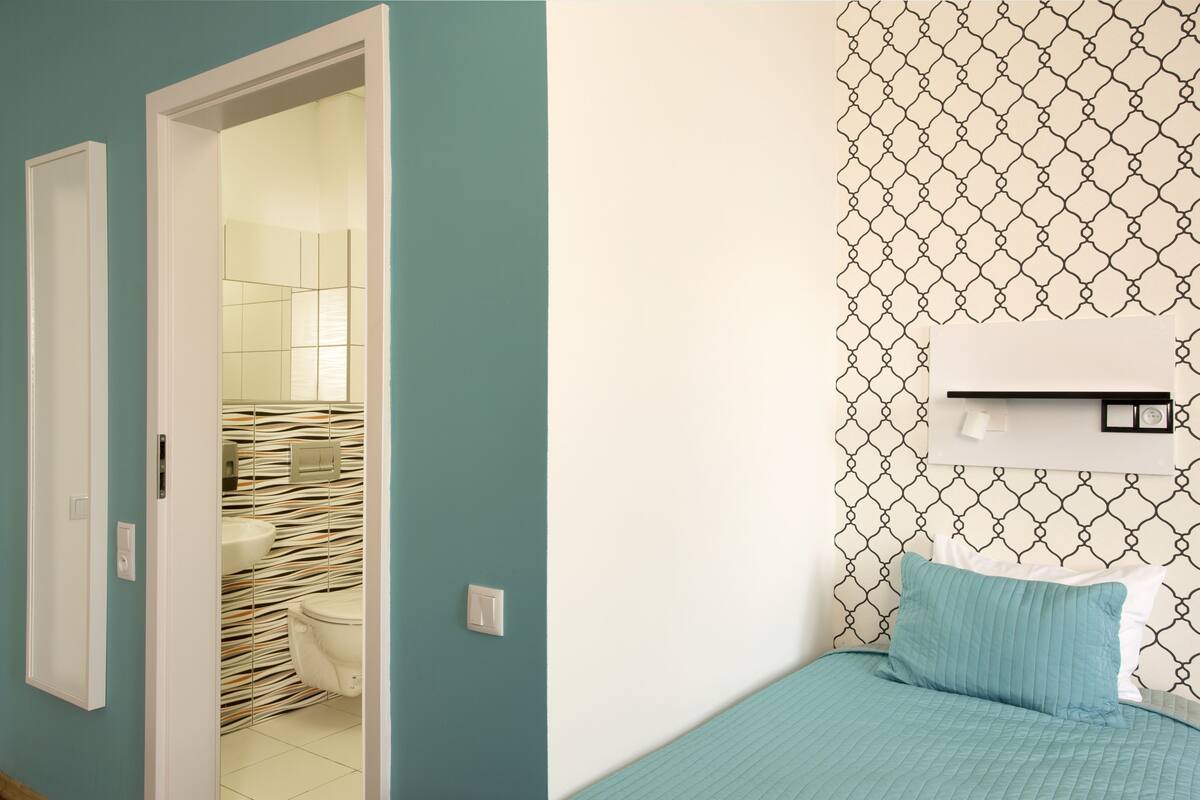 Quarto com cama, mesa de cabeceira e prateleira na parede.