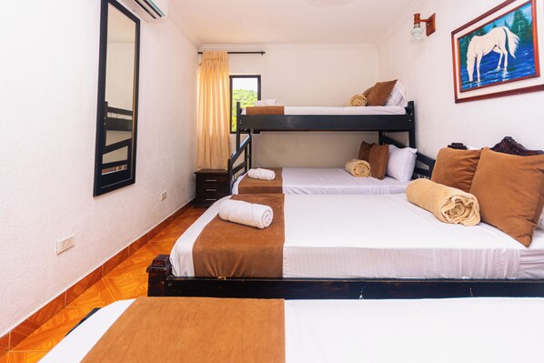 Quarto de hotel com duas beliches, um espelho, um quadro e uma janela com cortinas.