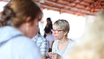Um grupo de pessoas sentadas à mesa em área externa coberta, possivelmente um restaurante ou café.