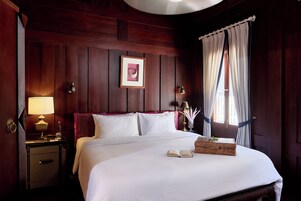 Cama bem arrumada com lençóis brancos, mesa de cabeceira com abajur e quadro na parede.