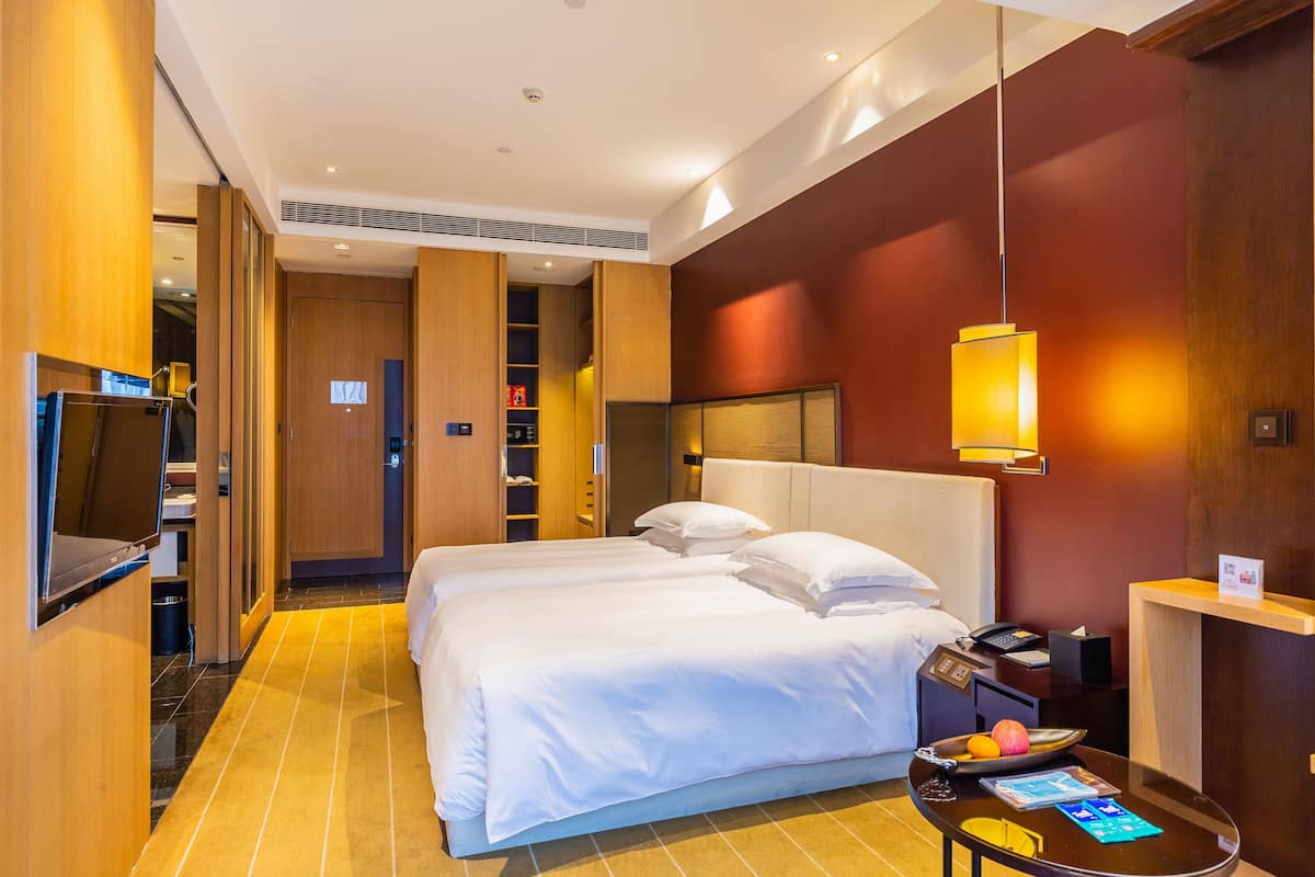 Quarto de hotel com uma cama grande, mesa de cabeceira com abajur, televisão presa na parede e guarda-roupa de madeira.