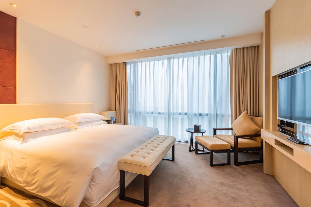 Quarto de hotel com uma cama grande, uma escrivaninha, uma cadeira e uma televisão.