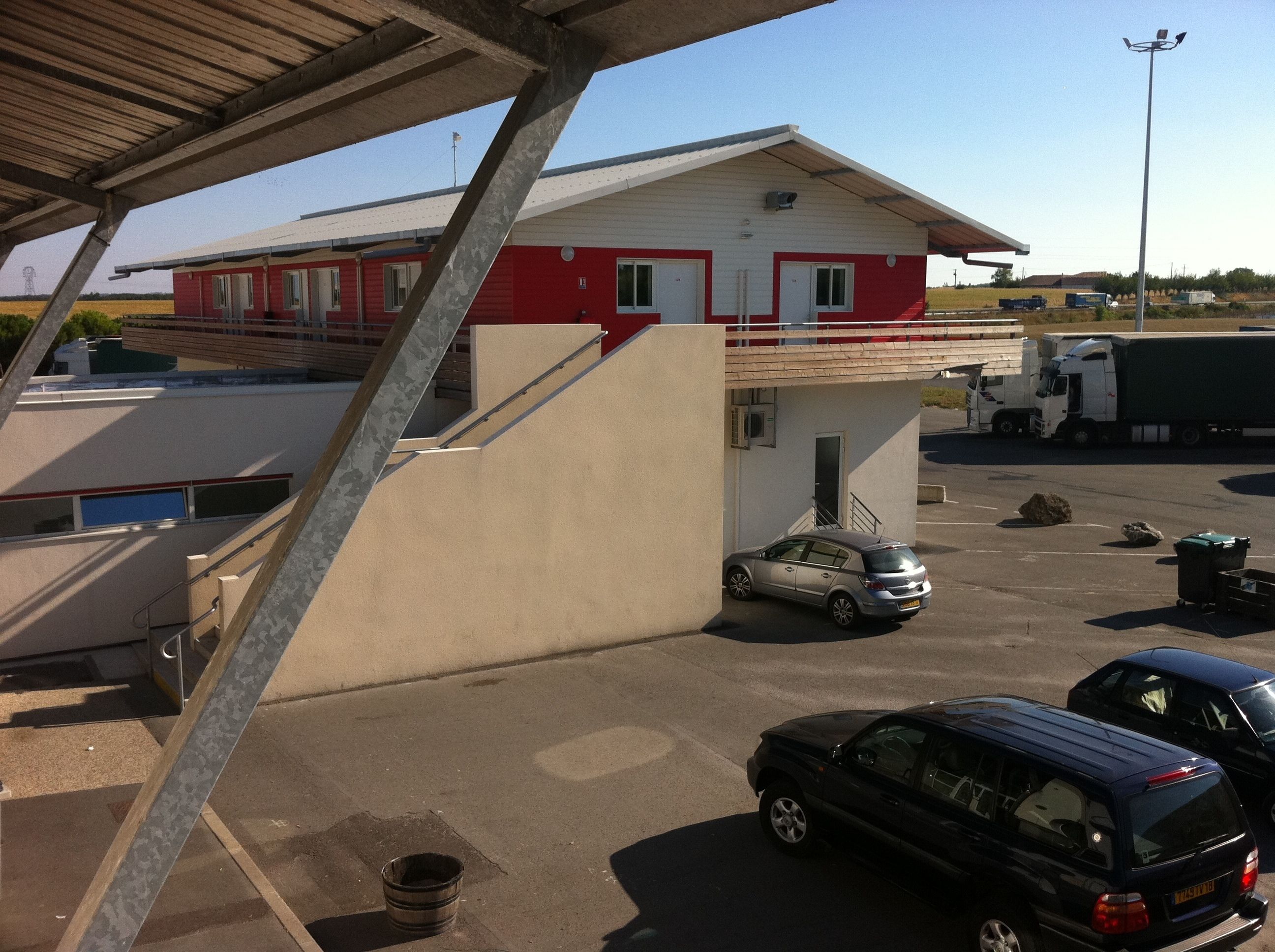 Um estacionamento com um edifício vermelho e branco, um caminhão e um carro.