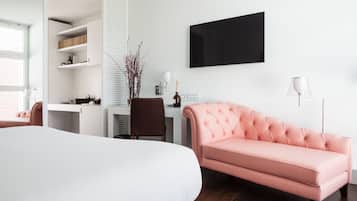 Quarto moderno com uma cama grande, um sofá rosa, uma escrivaninha com cadeira, uma TV na parede e uma janela com persianas.