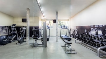 Uma academia com esteiras, elípticos, bancos de musculação e uma estrutura de halteres.