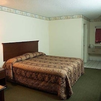 Quarto de hotel padrão com uma cama de solteiro, mesa de cabeceira, cômoda e banheiro com espelho e pia.
